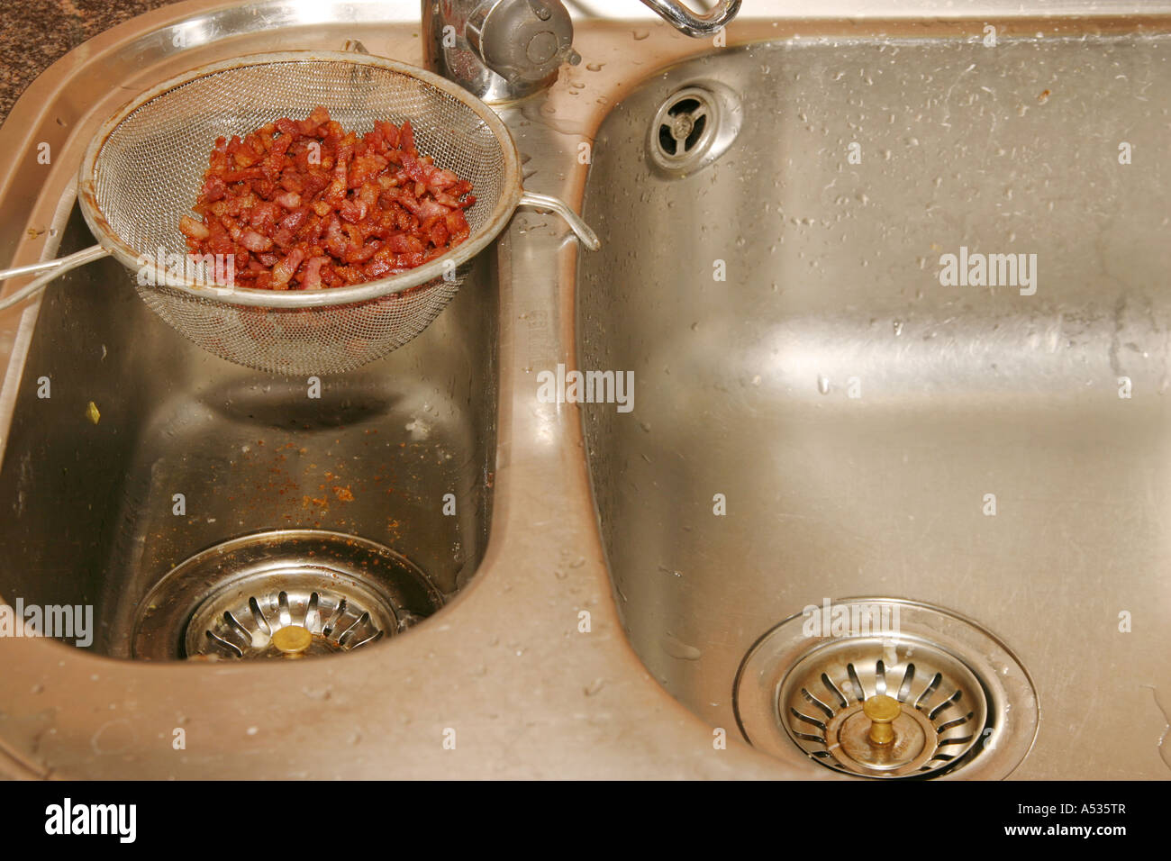 Close up of small pieces of bacon in a sieve. Fat dripping off into the ...