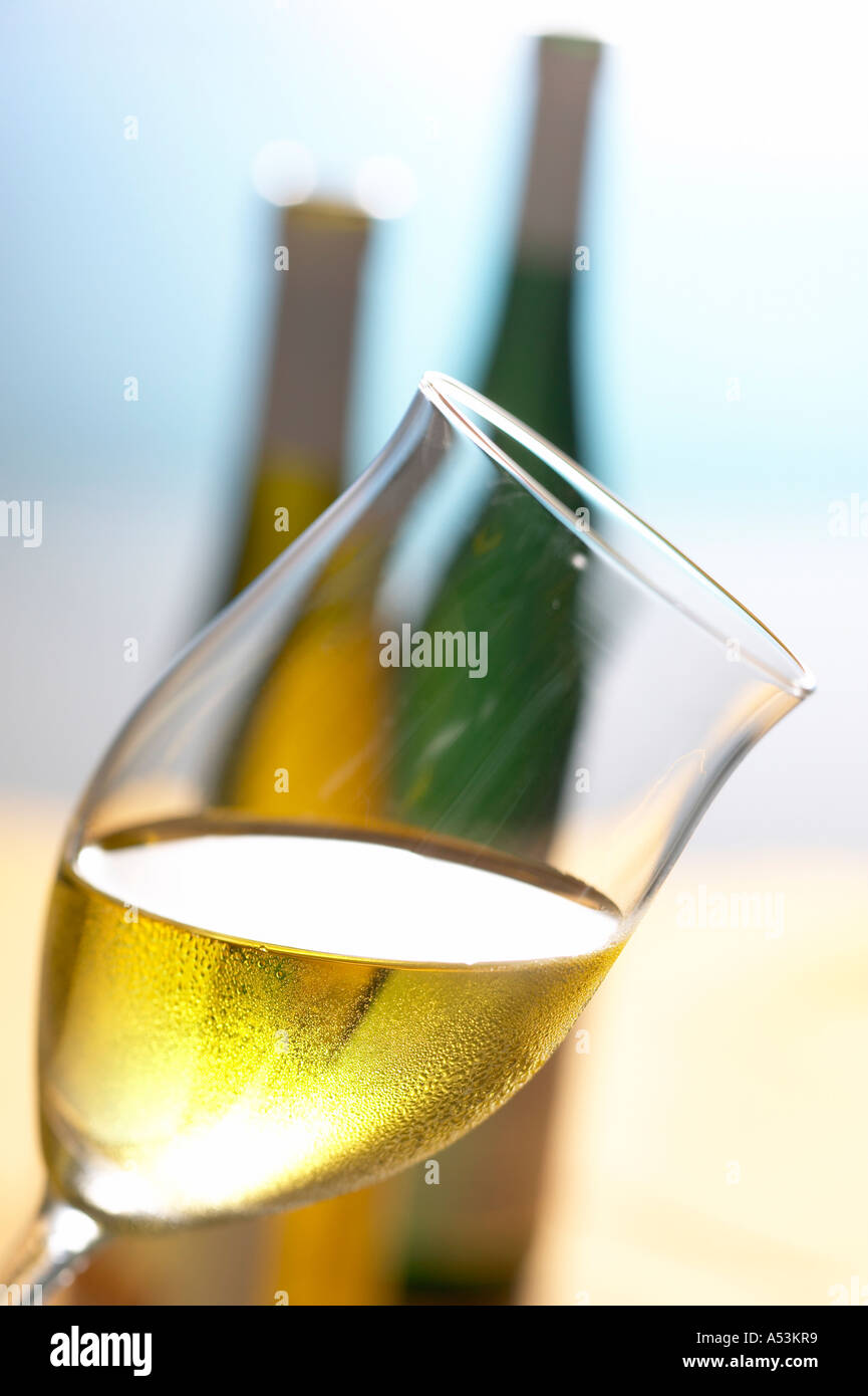 Glass of white wine held at an angle in front of two bottles Stock ...