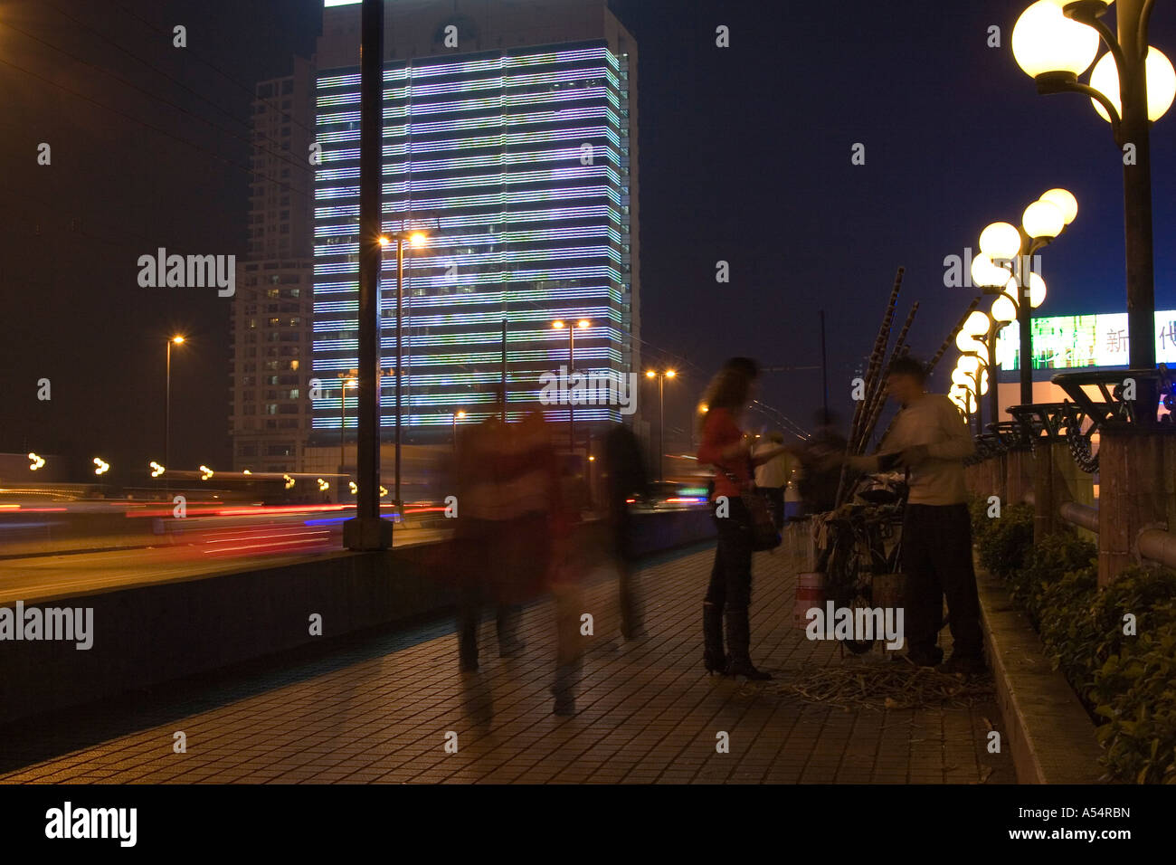 Sugar cane vendor with passing traffic and lit up building on a bridge ...