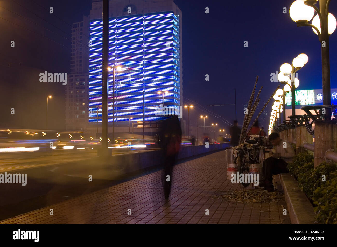 Sugar cane vendor with passing traffic and lit up building on a bridge ...