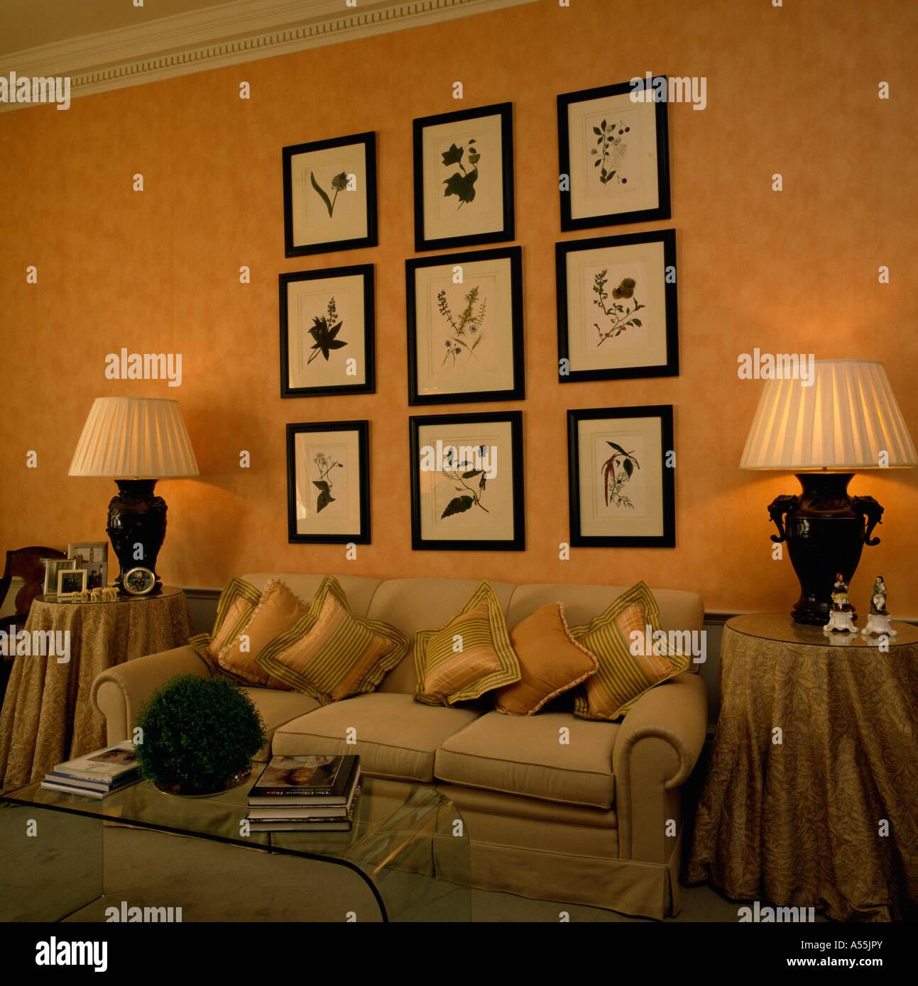 Group of pictures above beige sofa between tables with lighted lamps ...