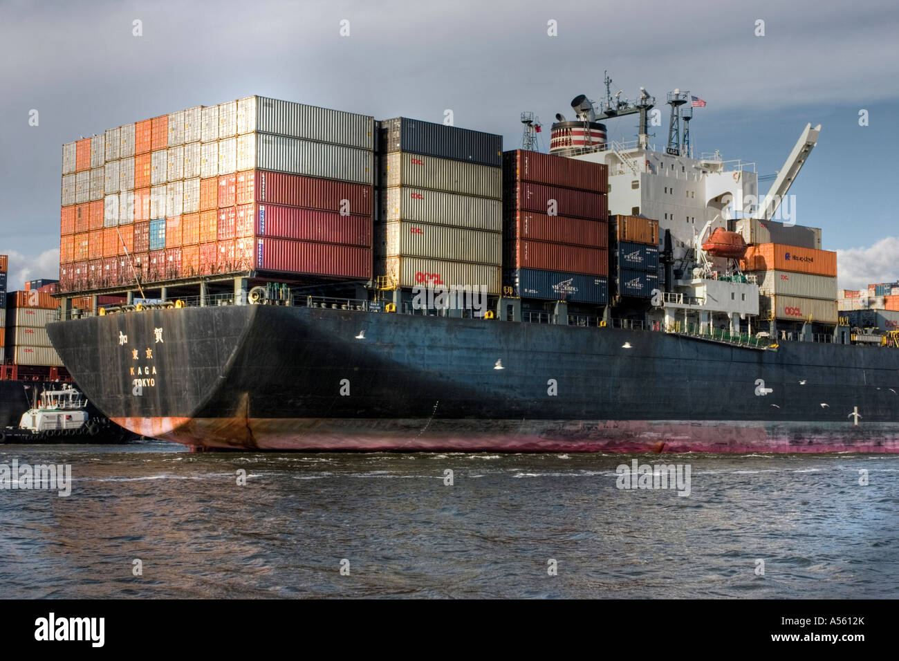 A large cargo ship loaded with shipping containers escorted by a ...