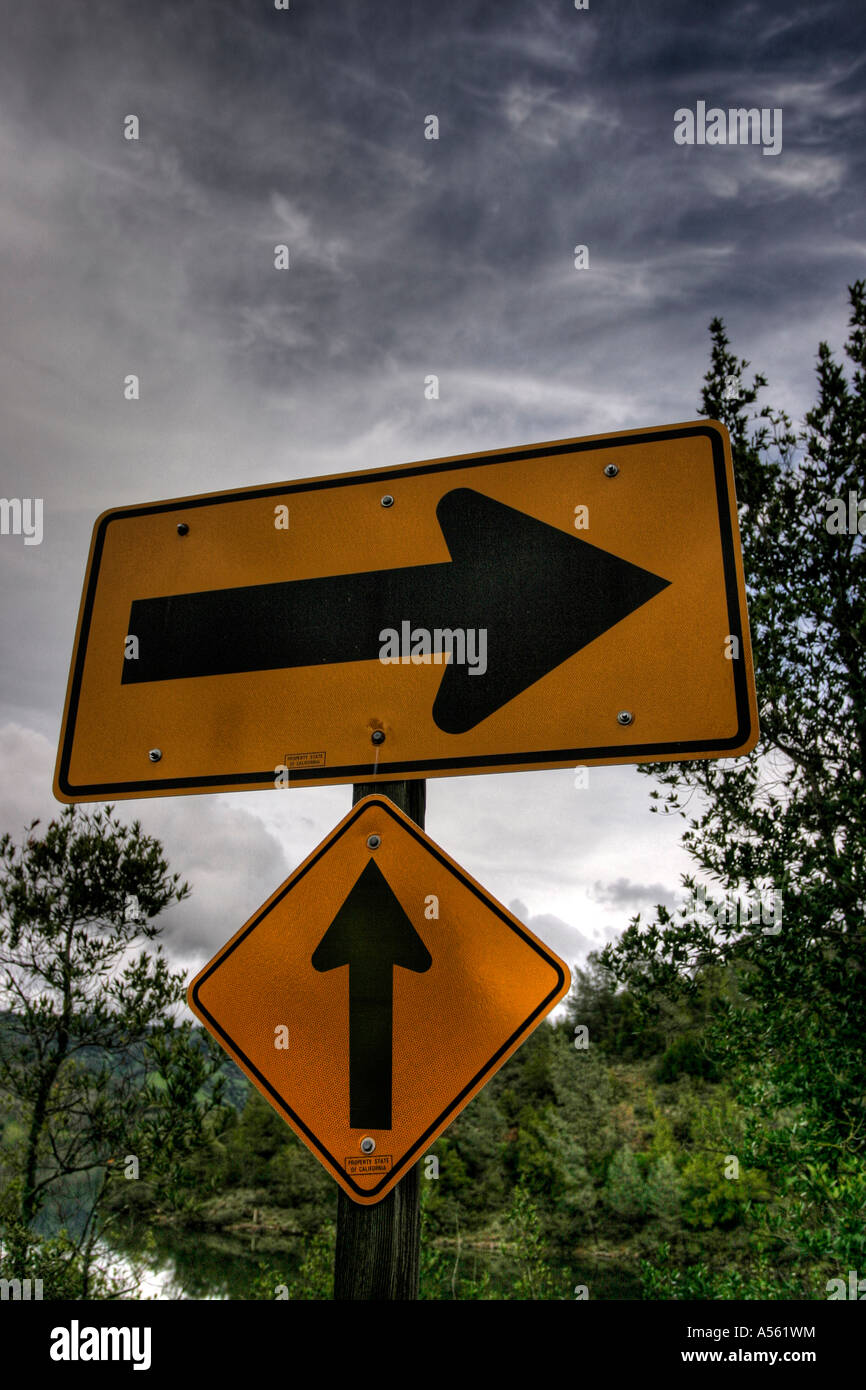 Two orange arrow road signs stand prominently against an overcast sky ...