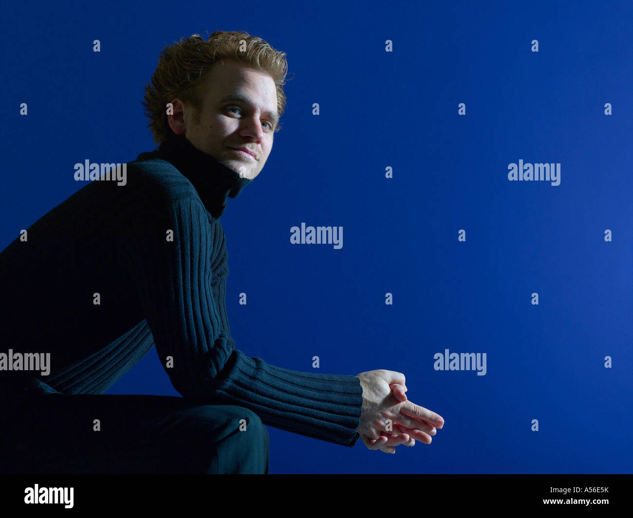 Young man sitting against blue background, portrait Stock Photo - Alamy
