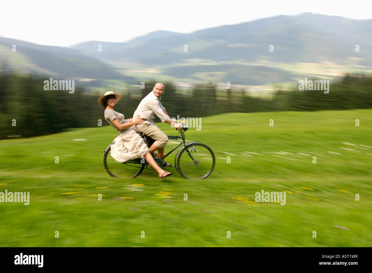 Couple riding bicycle in meadow, side view Stock Photo - Alamy