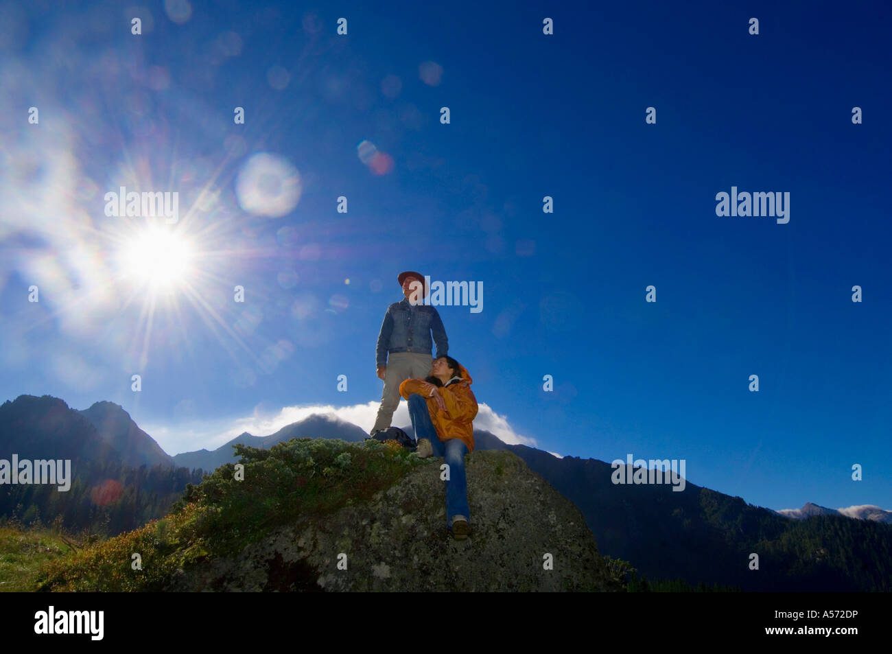 Couple in mountains, man standing, woman sitting on rocks Stock Photo ...