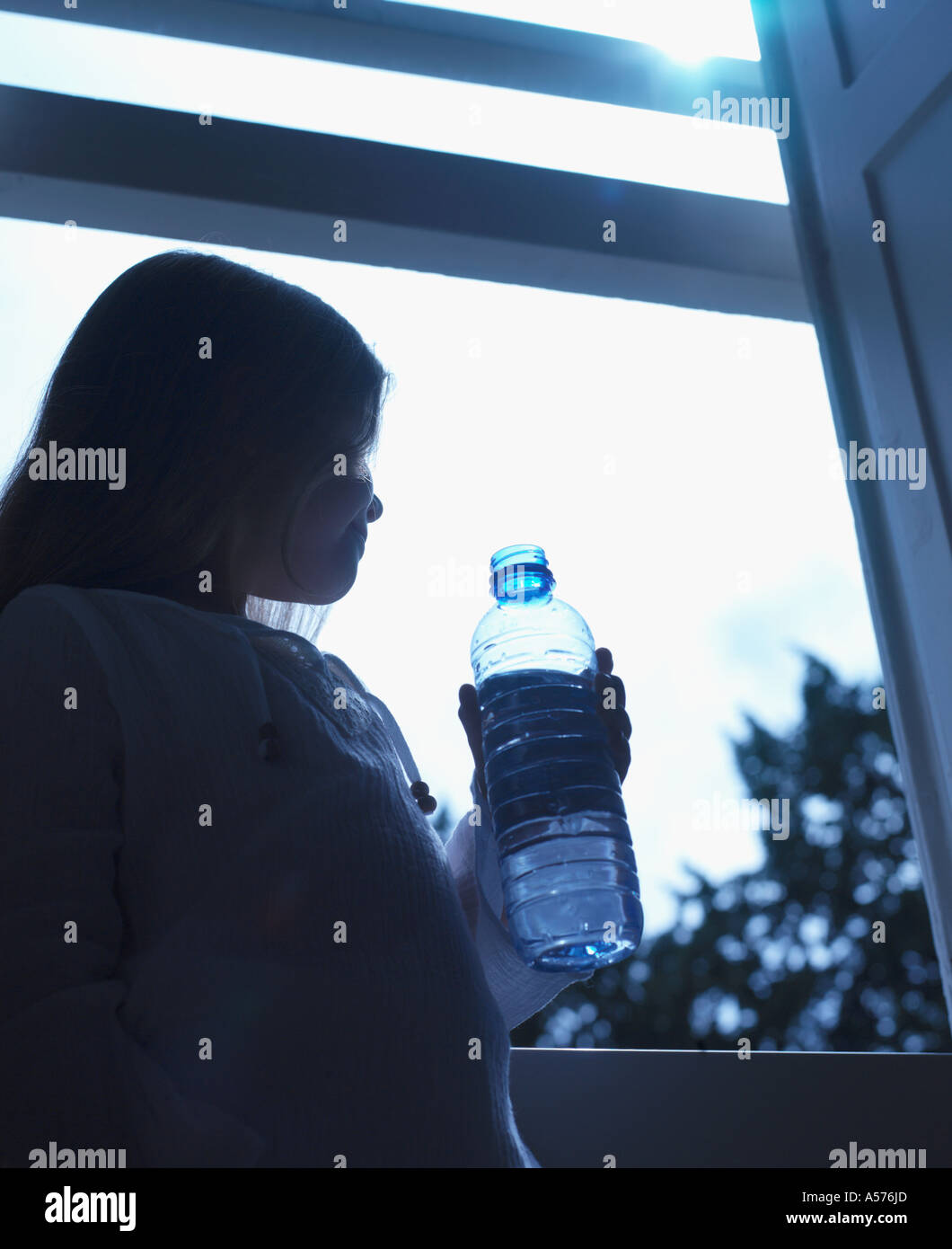 Girl holding a bottle of water looking outside a window Stock Photo - Alamy