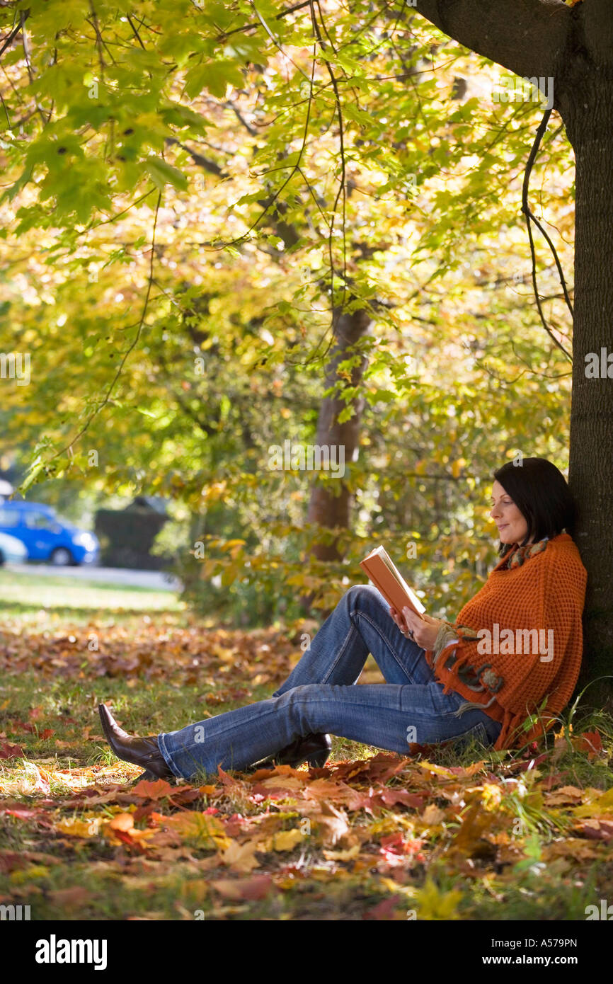 Woman sitting on tree, reading, side view Stock Photo - Alamy