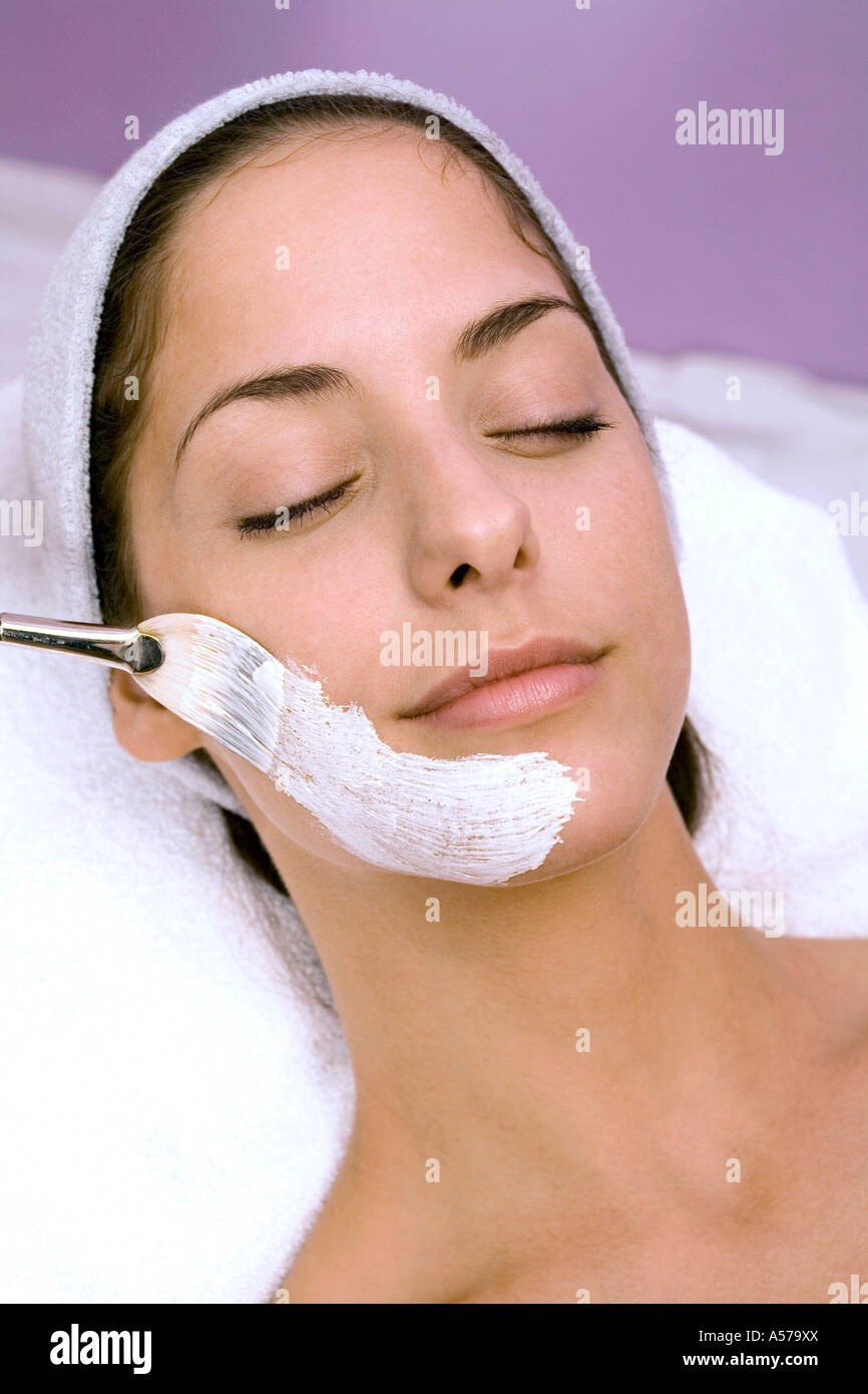 Young woman having face mask applied with make-up brush, eyes closed ...