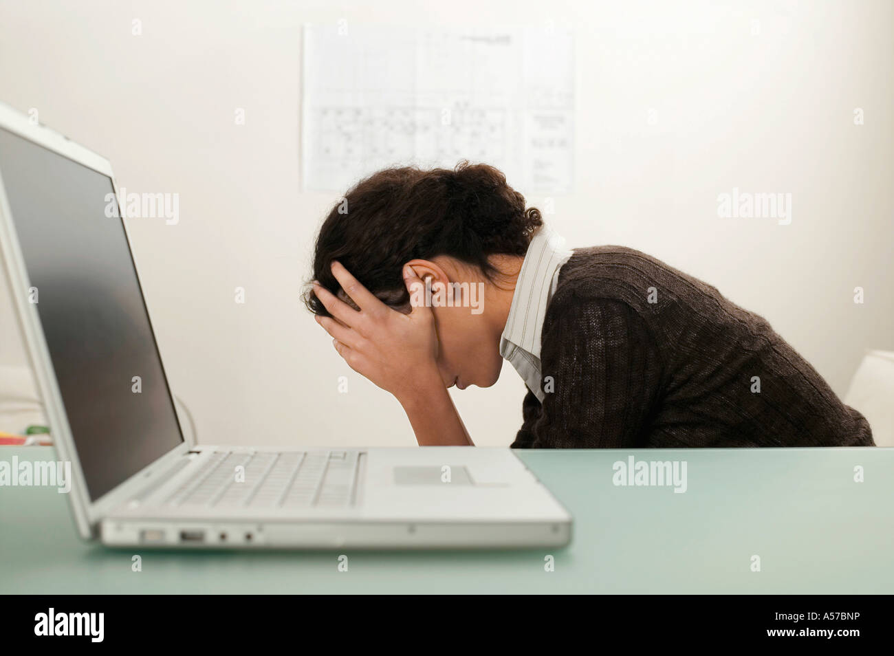 Young woman sitting on desk, hands on head, side view Stock Photo - Alamy