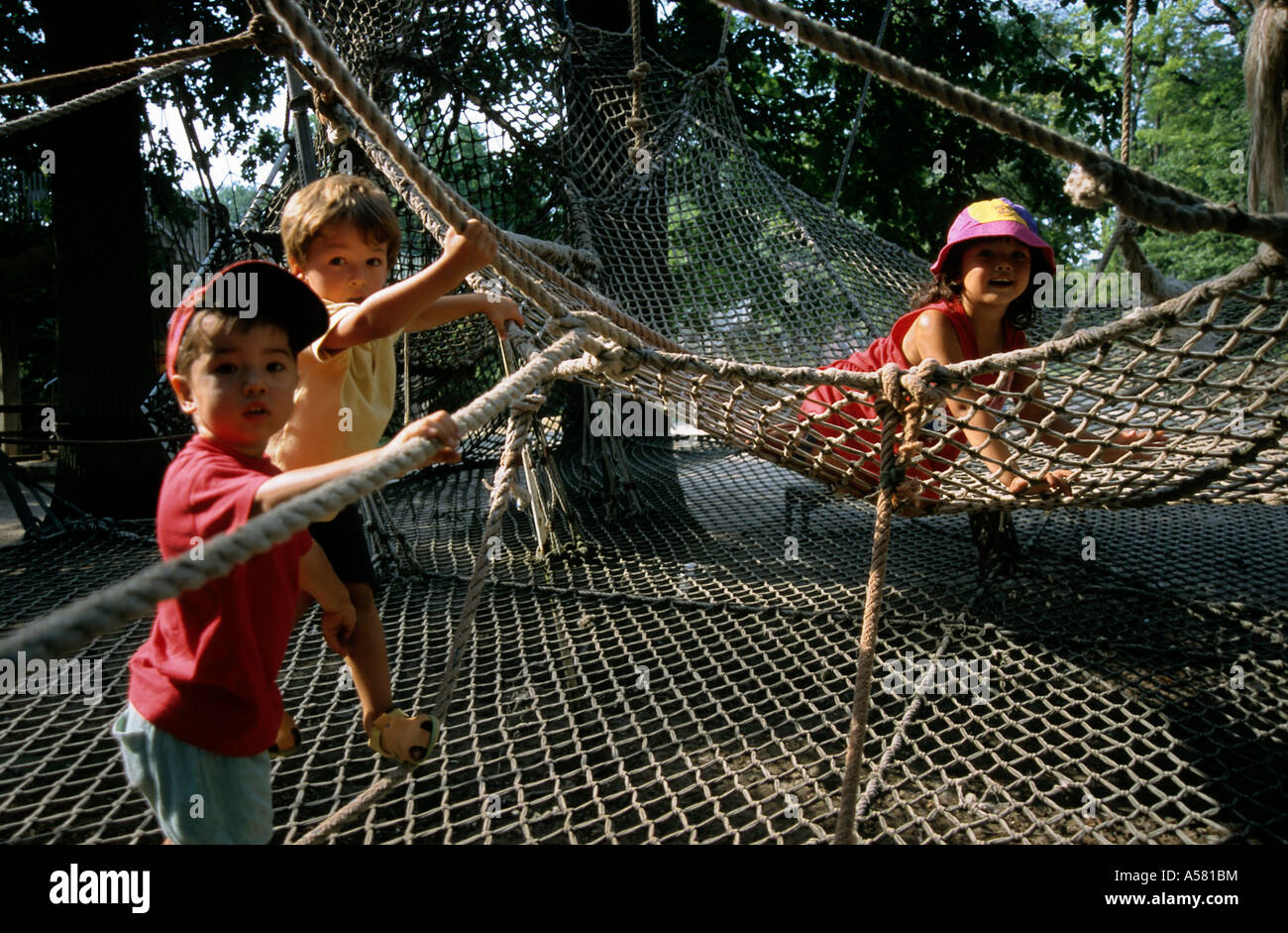 Three young children playing on a climbing net in a public park Stock ...