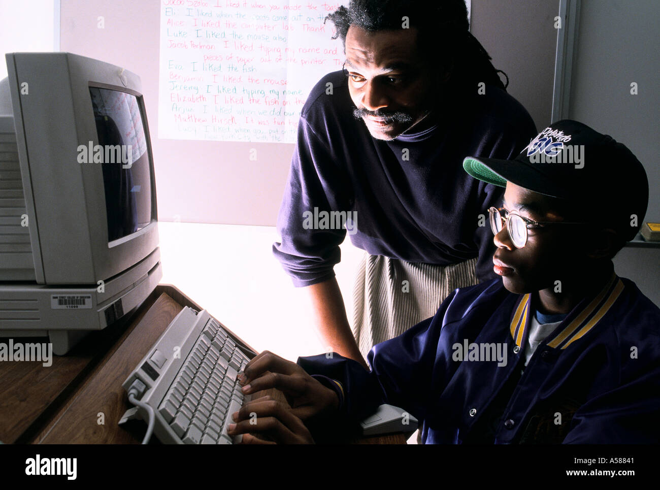 African American teacher looking over the shoulder of a student as he ...