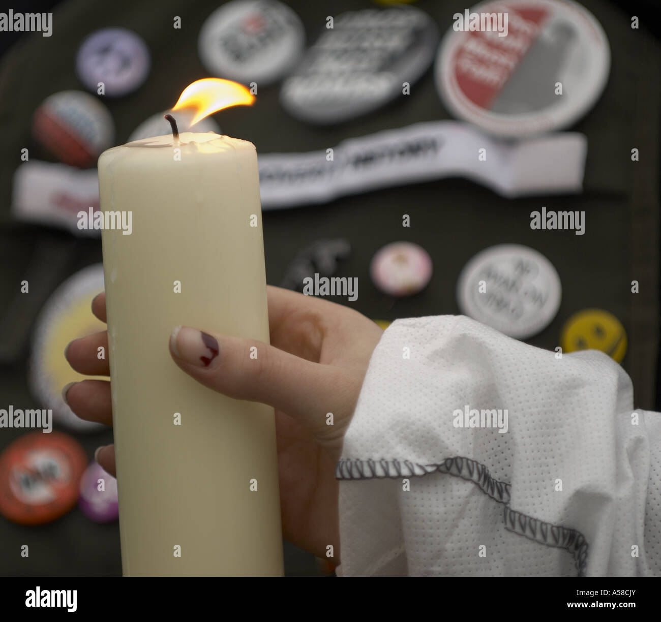 Woman's hand holding a lit pillar candle and peace badges at anti ...