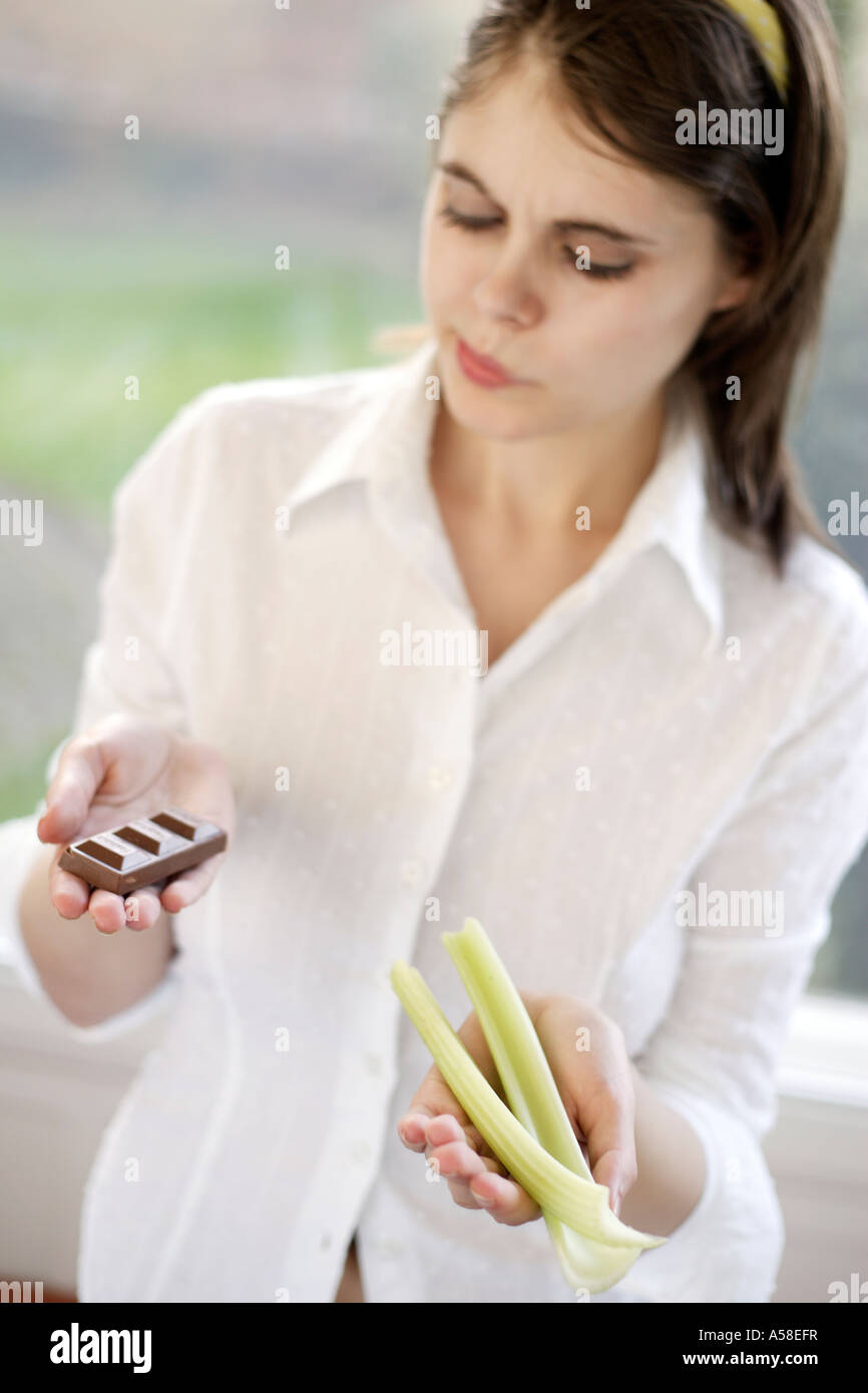 Girl deciding between chocolate and celery Stock Photo - Alamy