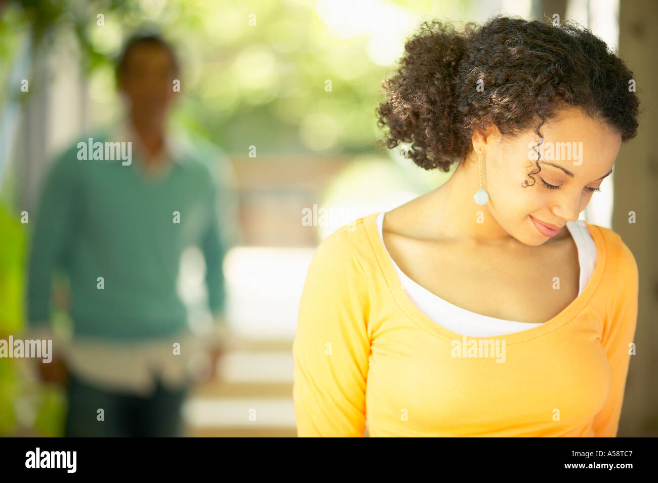 Woman looking down with man in background Stock Photo - Alamy