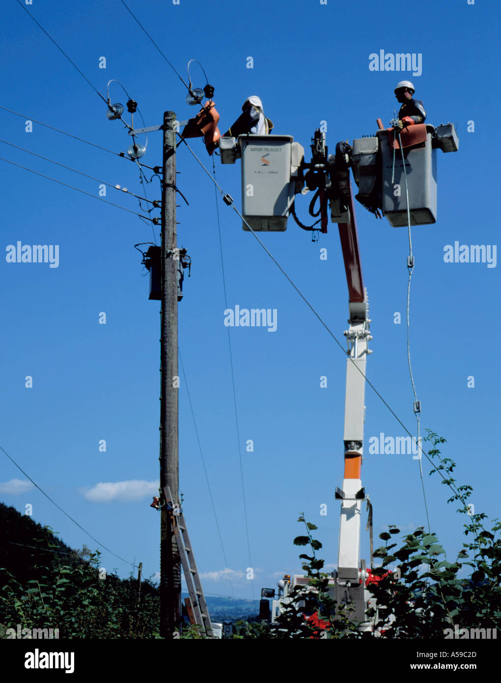 Linesmen repairing high voltage overhead power cables from a lorry ...