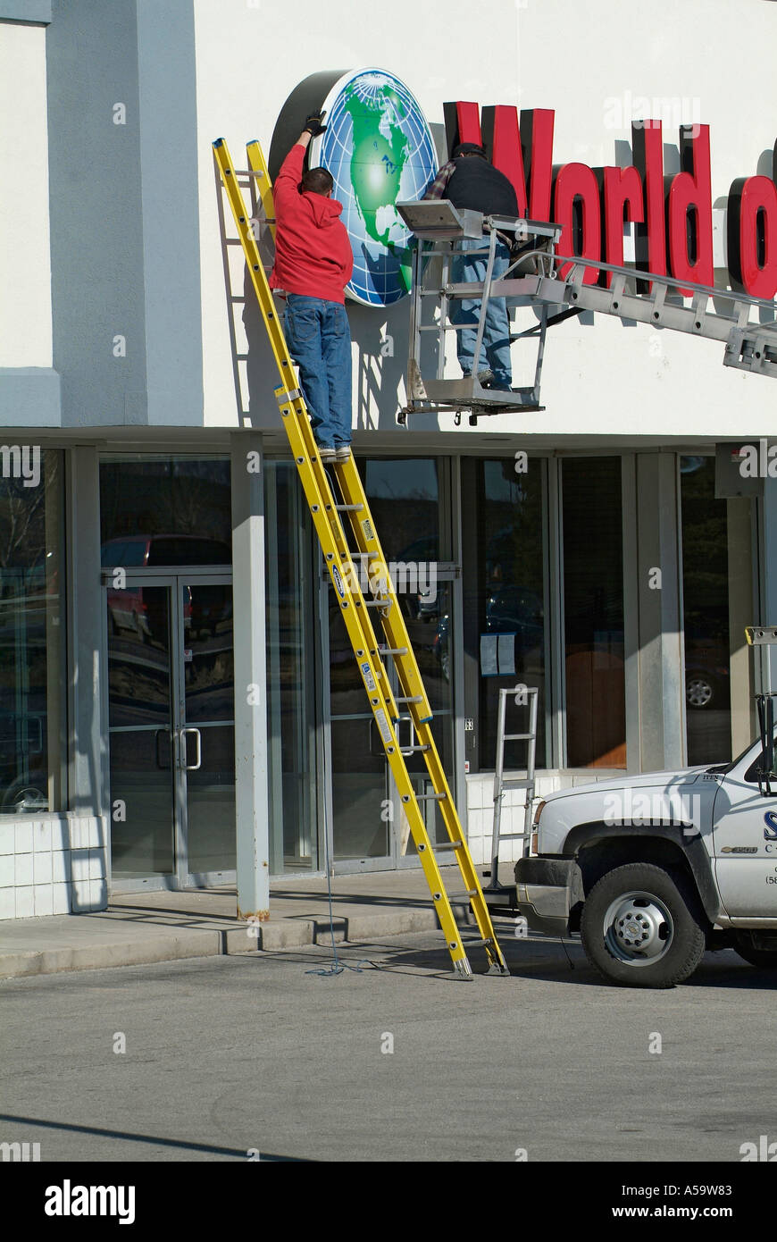 Two men climb ladder to install sign on a business front Stock Photo ...