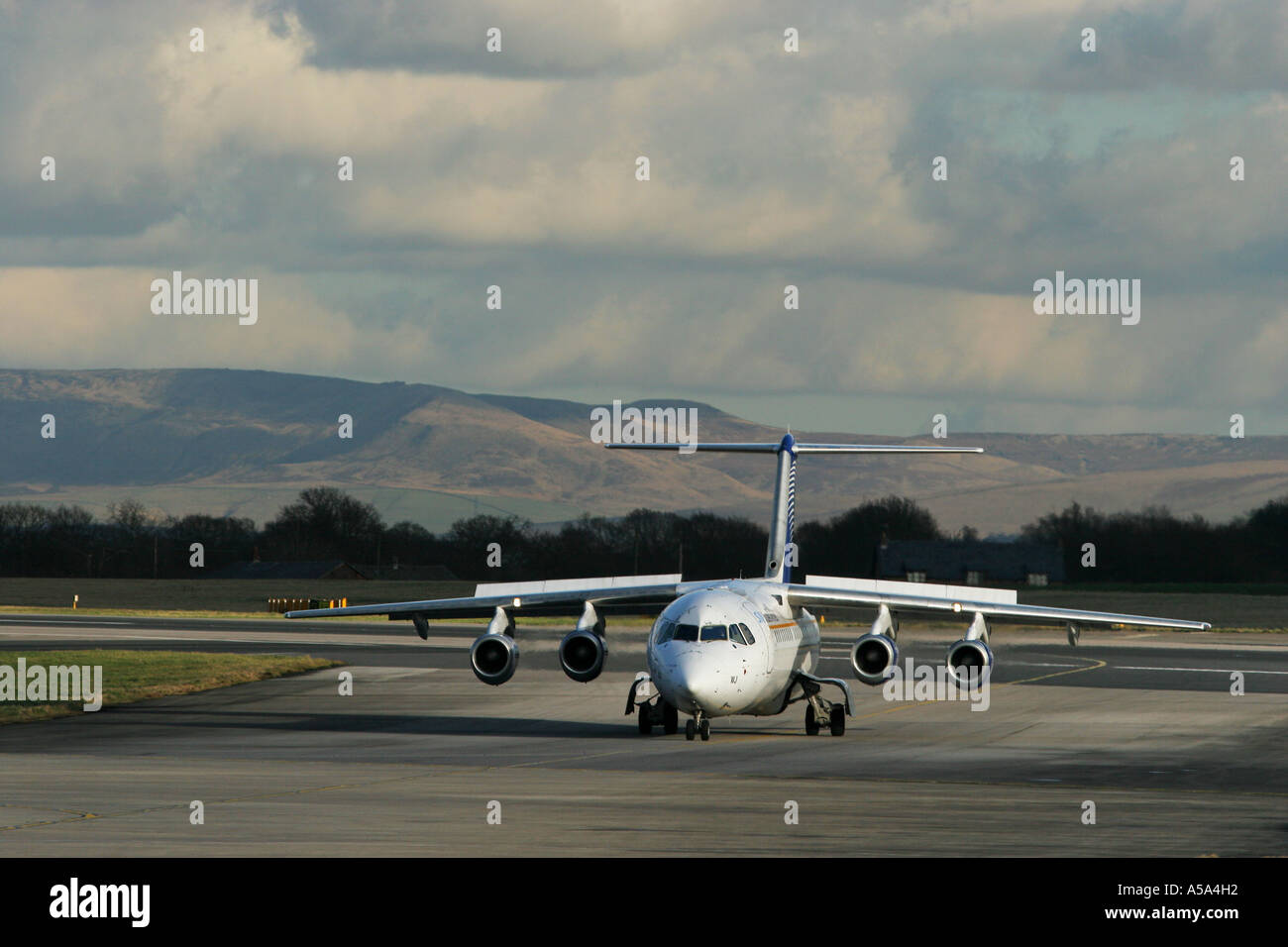A jet plane taxis over the runway at Manchester Airport. The hills of ...