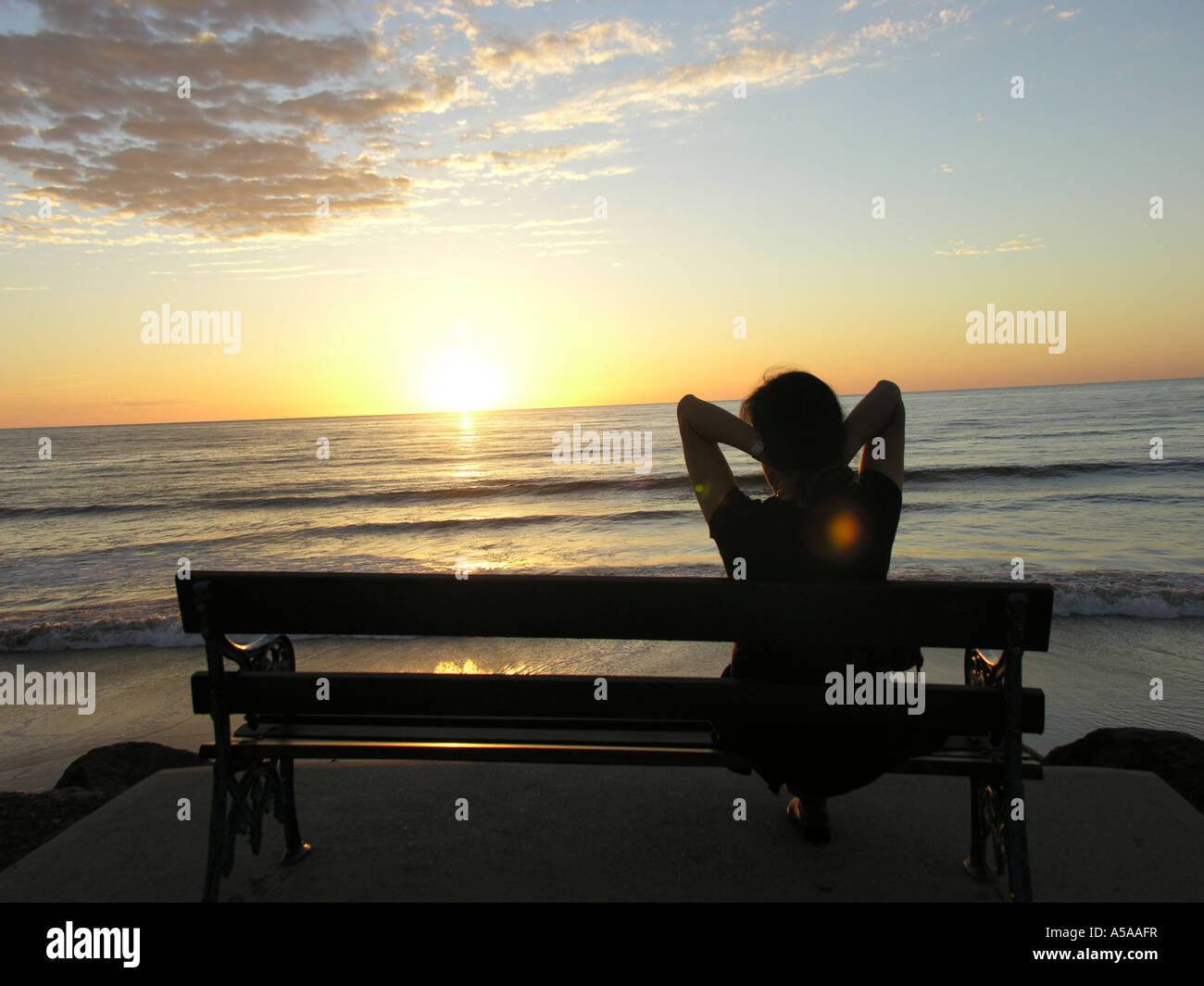 Young woman sitting on bench watching sunset over sea Stock Photo - Alamy