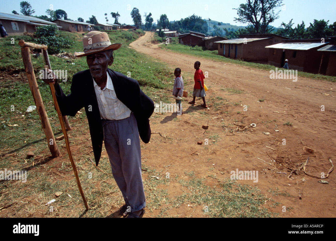 Elderly man with walking stick in village, children in background ...