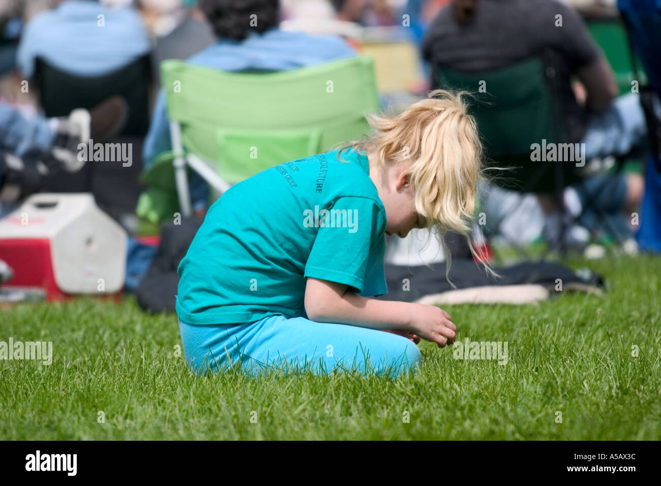 Young blond girl part of a crowd at a concert sitting on the grass ...