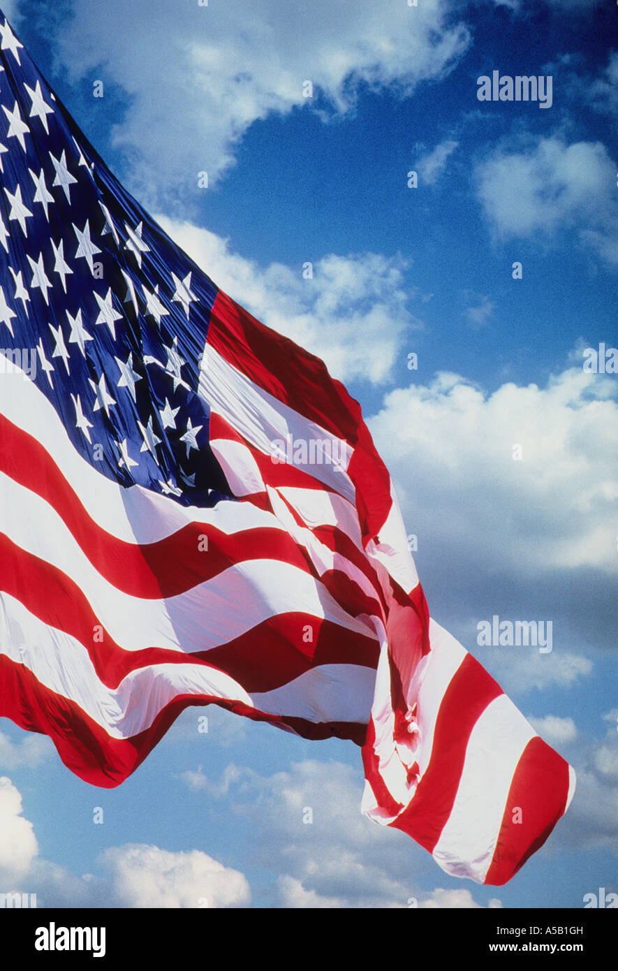 American flag flying in the wind outdoors against a blue sky and puffy ...