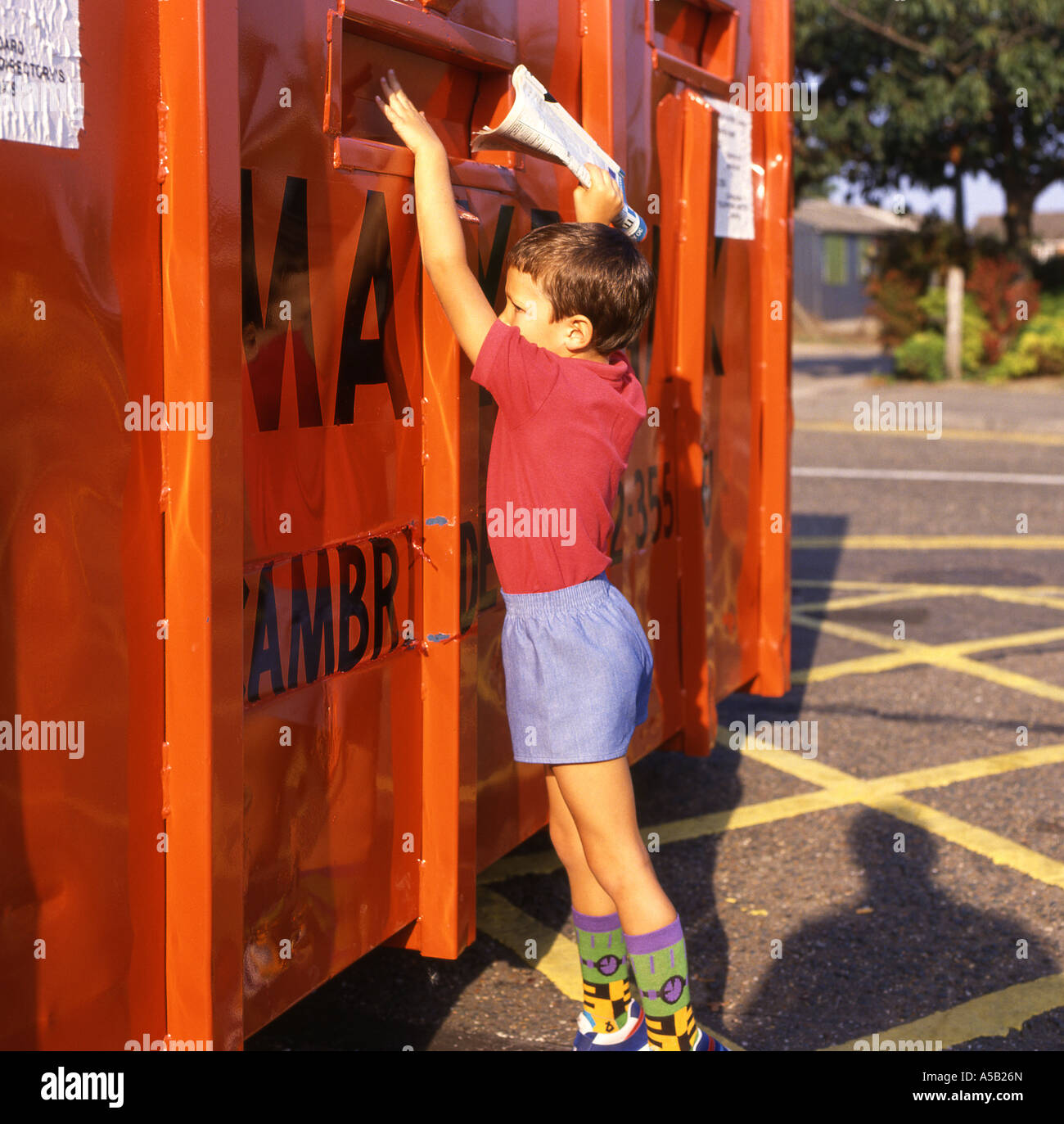 Young boy putting waste paper in recycling bank Stock Photo - Alamy