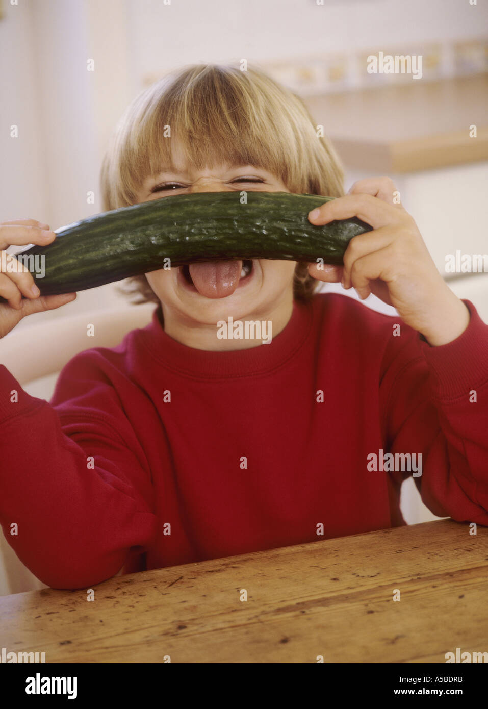 Young boy sitting in a kitchen, with a cucumber - having fun Stock ...