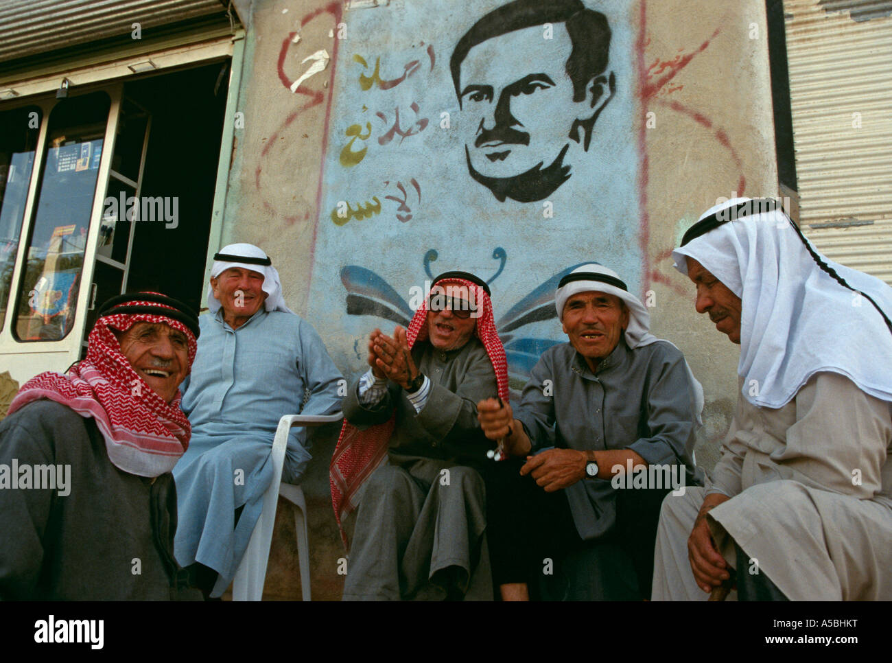 Men drinking coffee with a picture of Hafez Al'Assad in the background ...