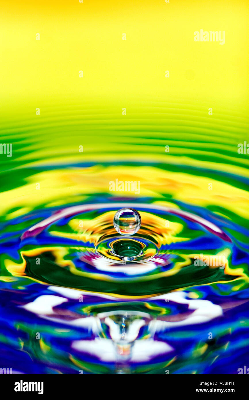 Multicoloured water drop and ripple. Water on a plate mirror with ...
