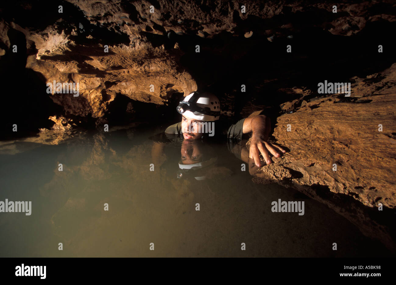 Caver crawling through a low passage through water Belize Central ...