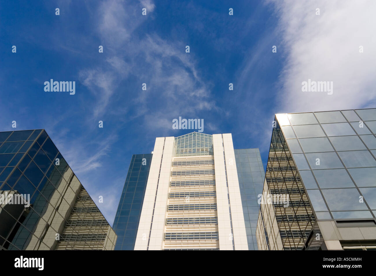 Glass fronted skyscrapers reach up into a bright blue sky with a few ...