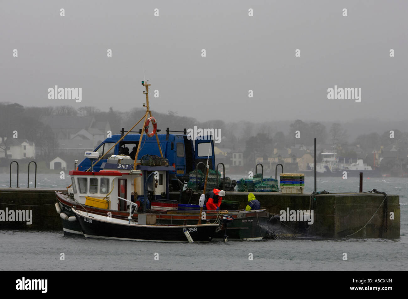small fishing boat unloading onto a pier with workers on deck on a ...