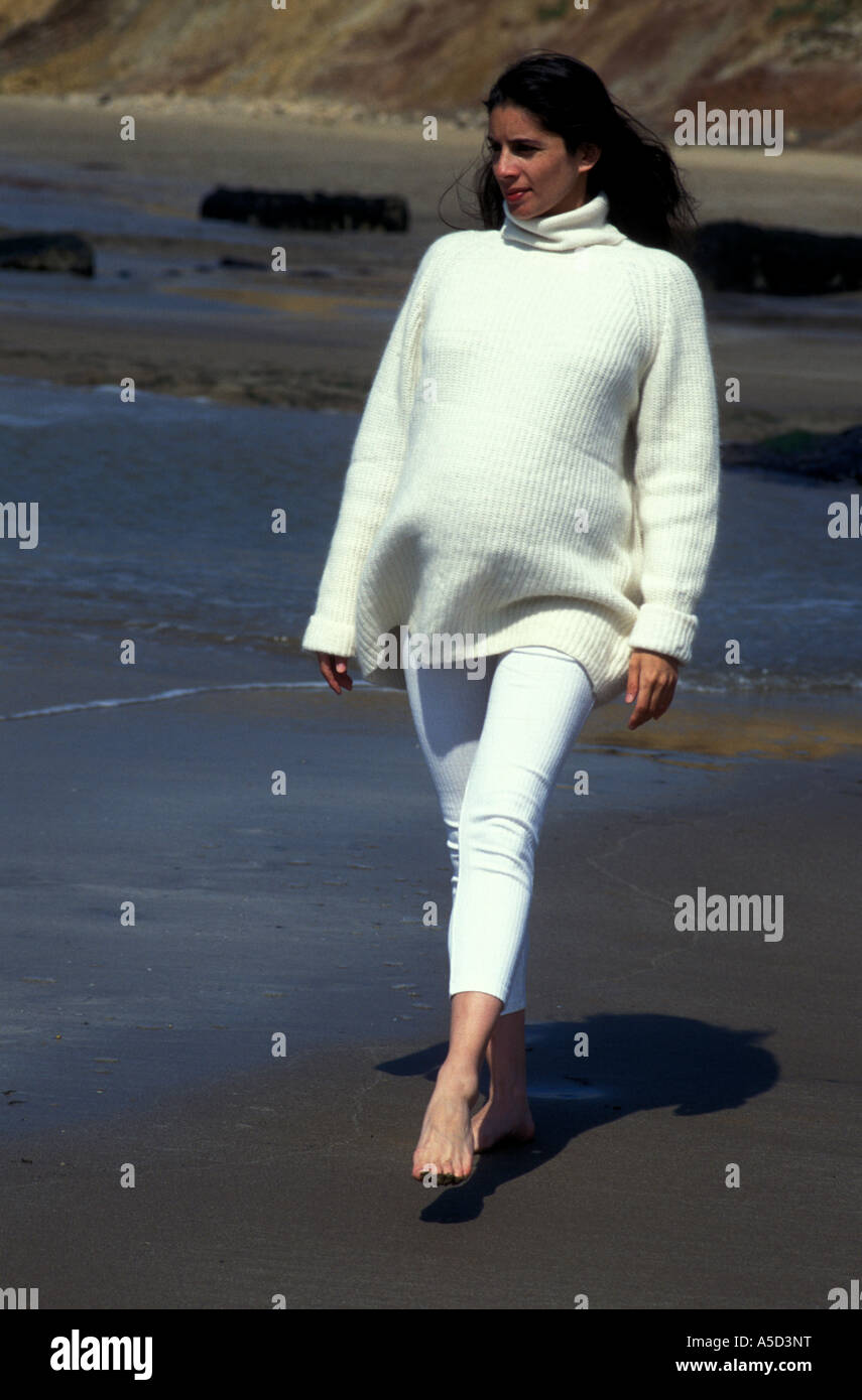 anglo asian pregnant woman dressed in white walking along beach on ...