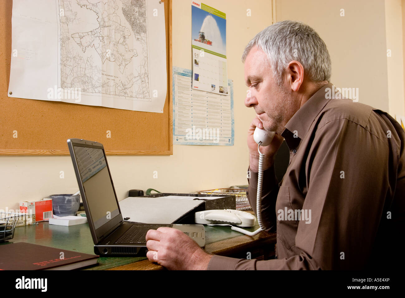 Farmer working in the farm office on paperwork using a laptop Stock ...
