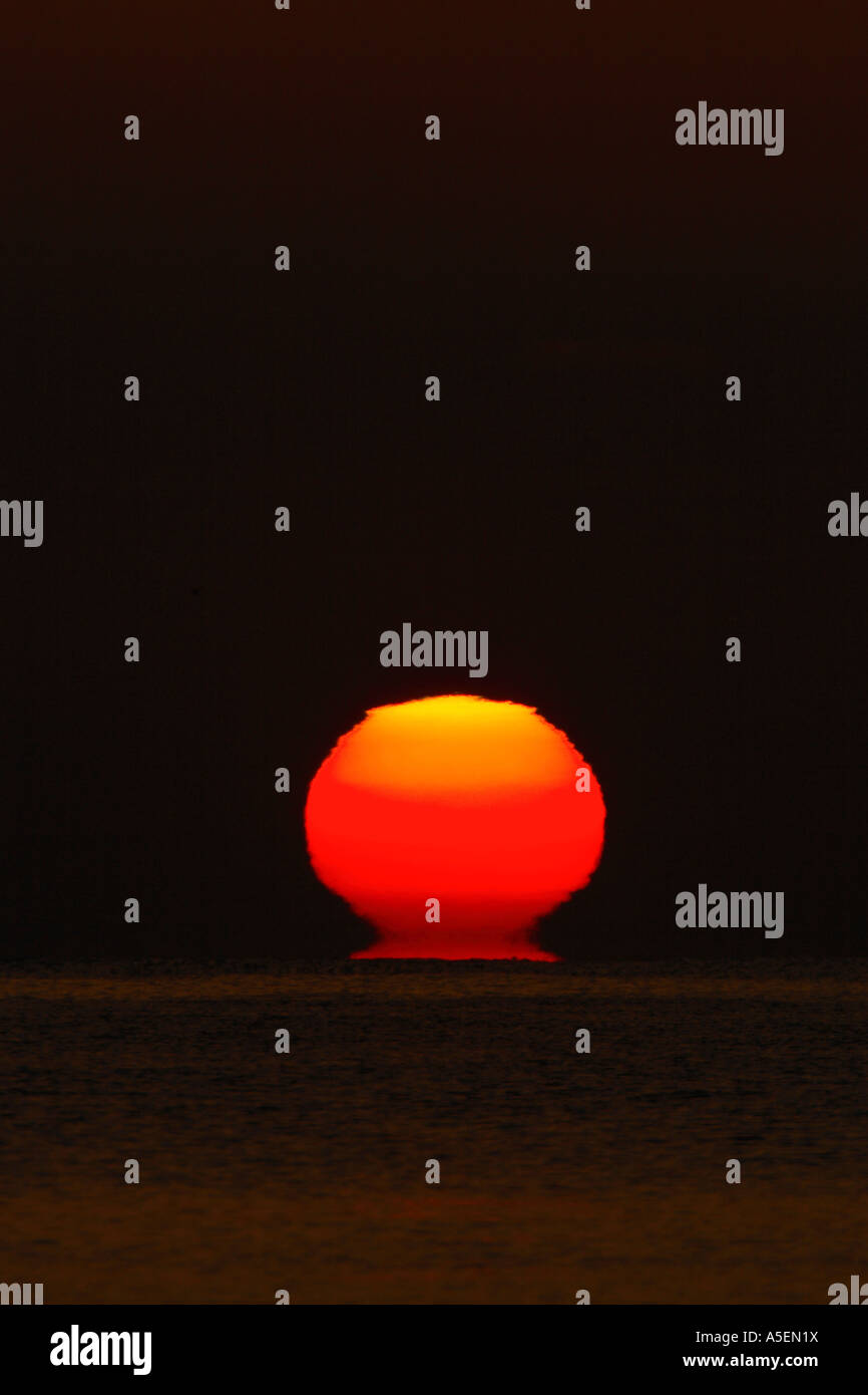 sun rising over sea coloured yellow and red distorted by atmospheric ...