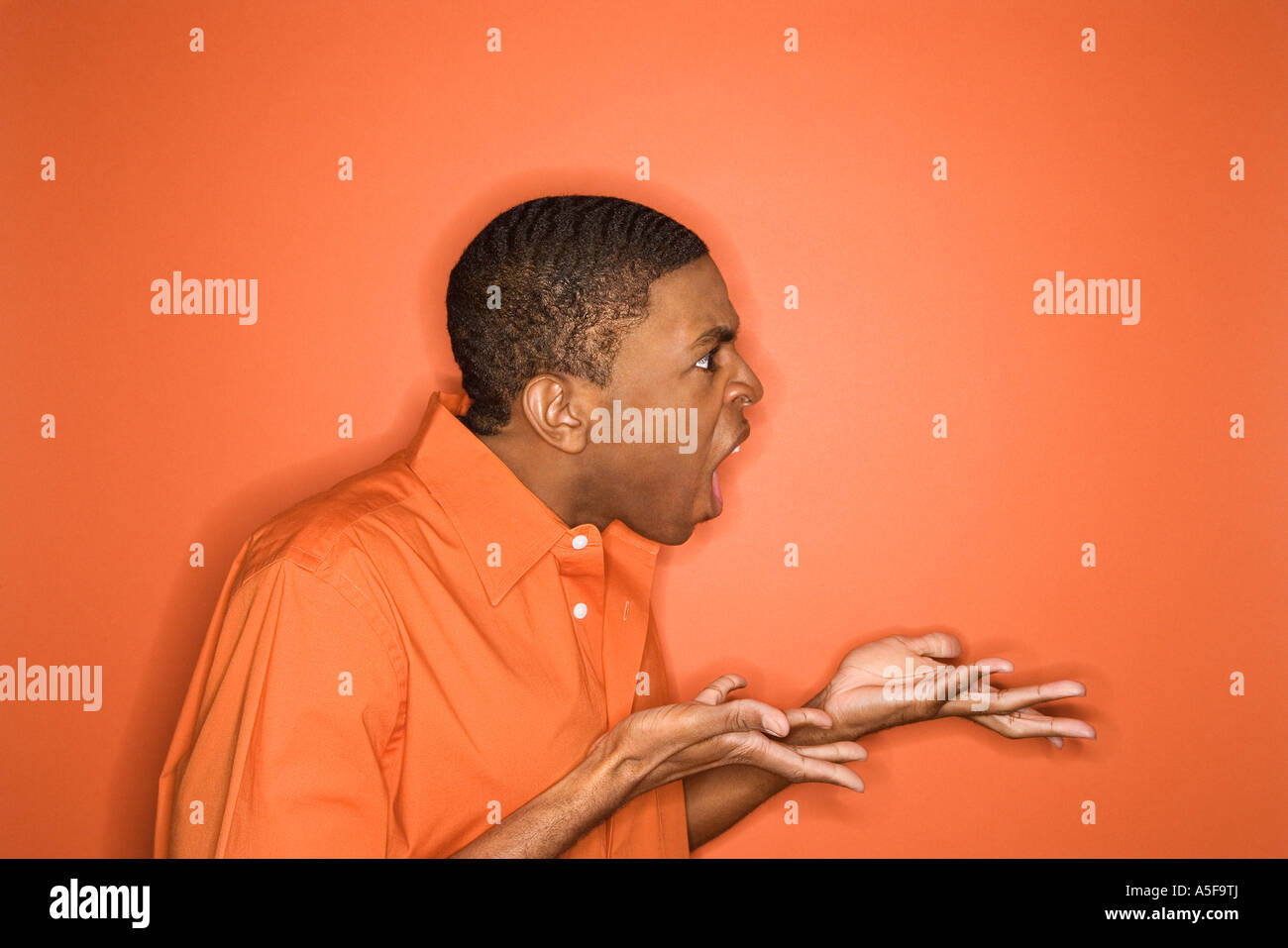 Side view of young African American man on orange background expressing ...