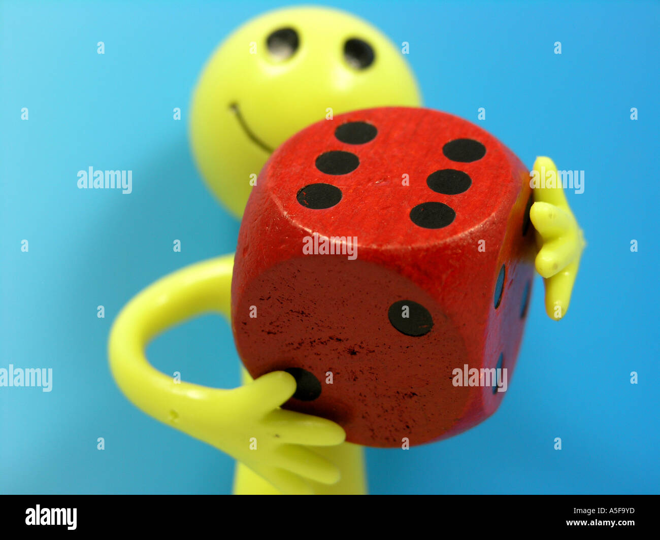 Yellow bendy rubber figure holding a red wooden dice Stock Photo - Alamy