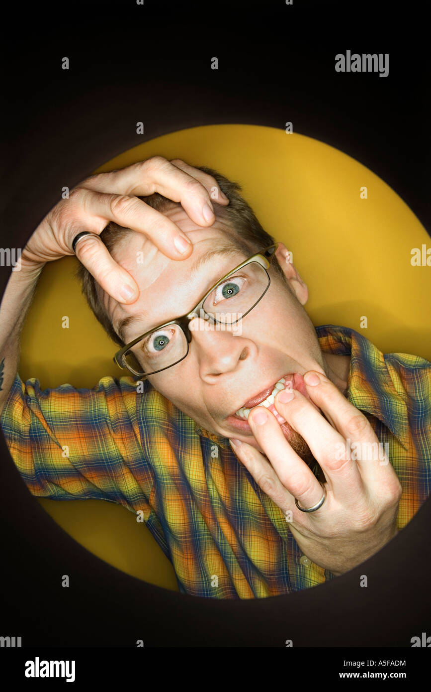 Vignette of adult Caucasian man on yellow background pulling at face ...