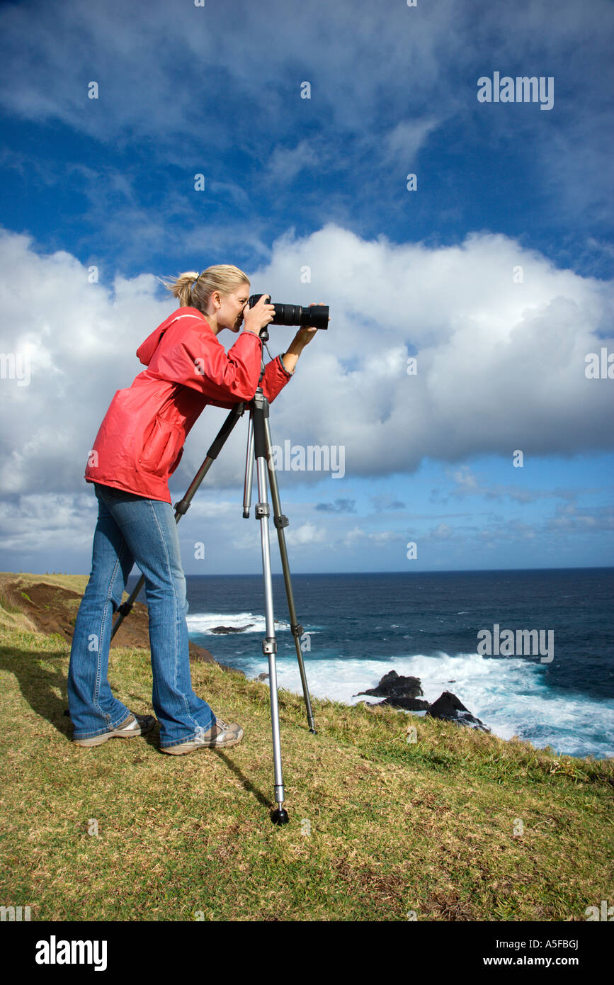 Caucasian mid adult woman looking through camera on tripod on cliff ...