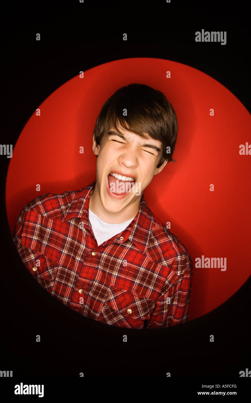 Portrait of Caucasian teen boy screaming with eyes closed against red ...