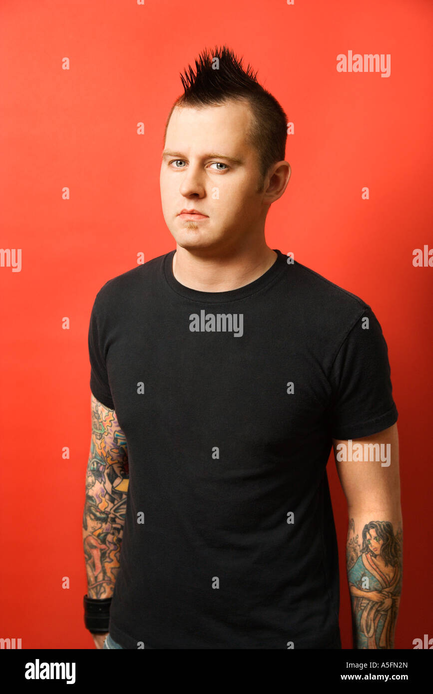 Caucasian man with mohawk and tattoos standing against orange ...
