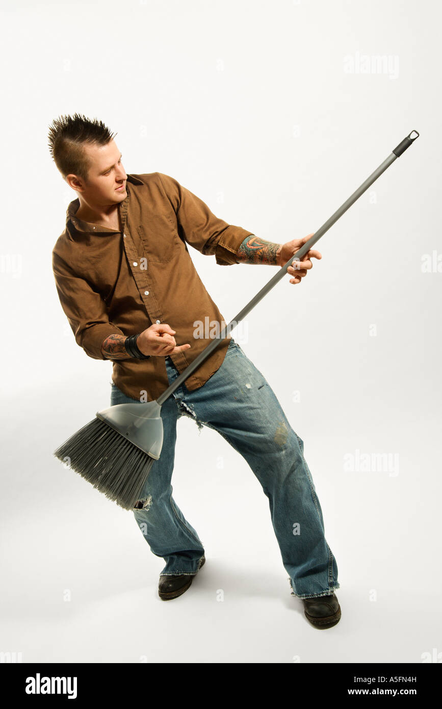 Caucasian man with mohawk playing broom like guitar against white ...