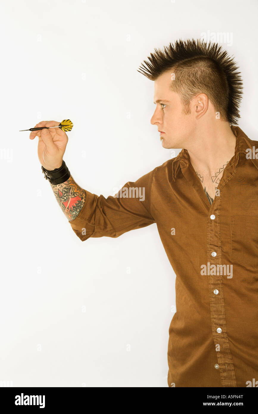 Side view of Caucasian man with mohawk holding and aiming dart against ...
