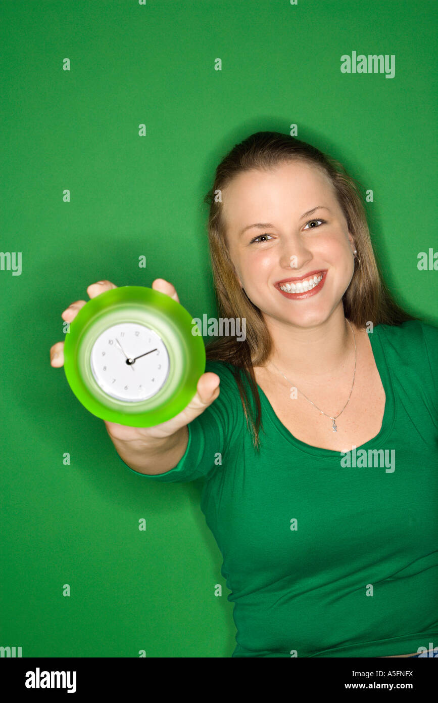 Caucasian young female adult holding out clock and smiling Stock Photo ...