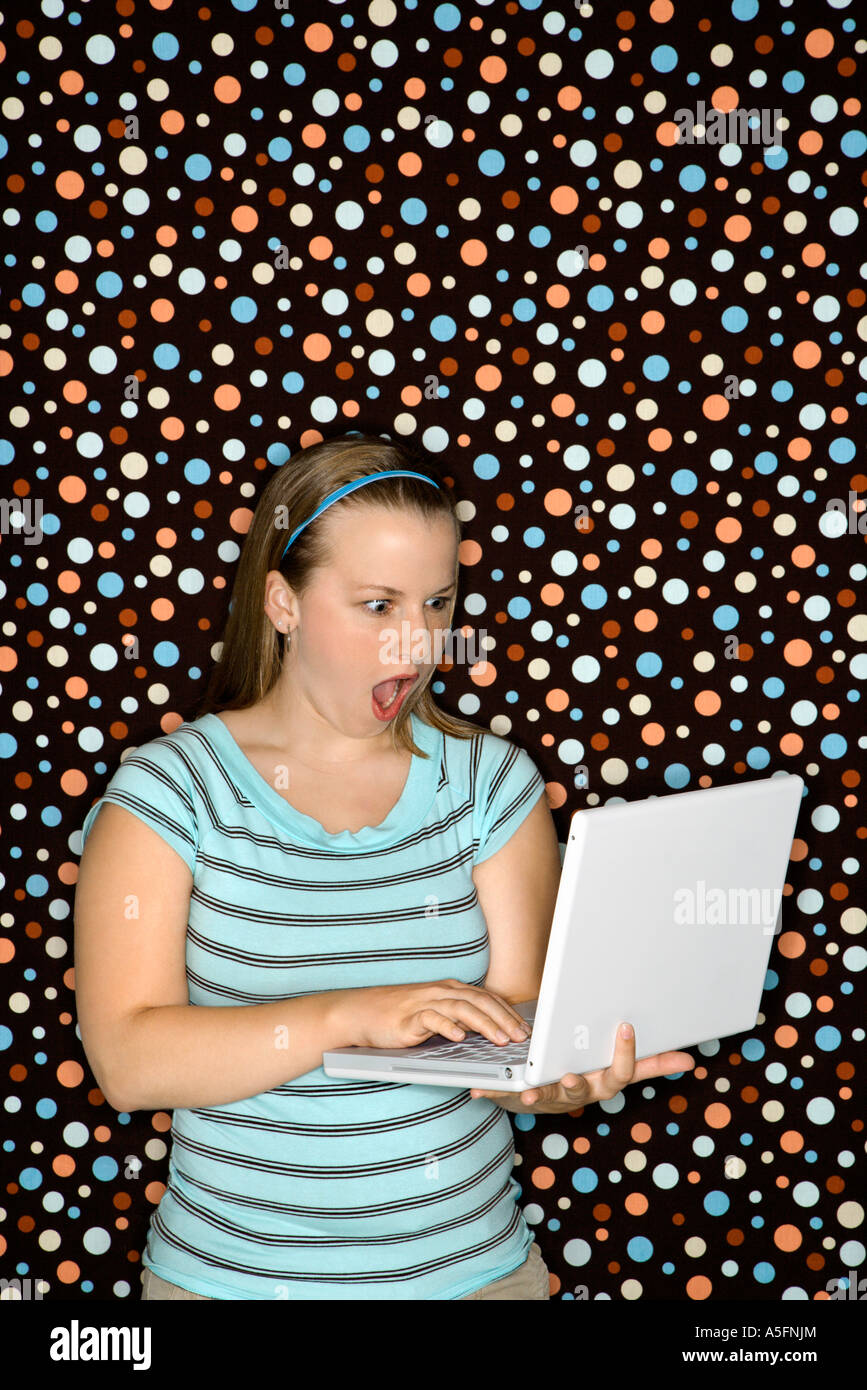 Young Caucasian woman typing on laptop and looking shocked Stock Photo ...