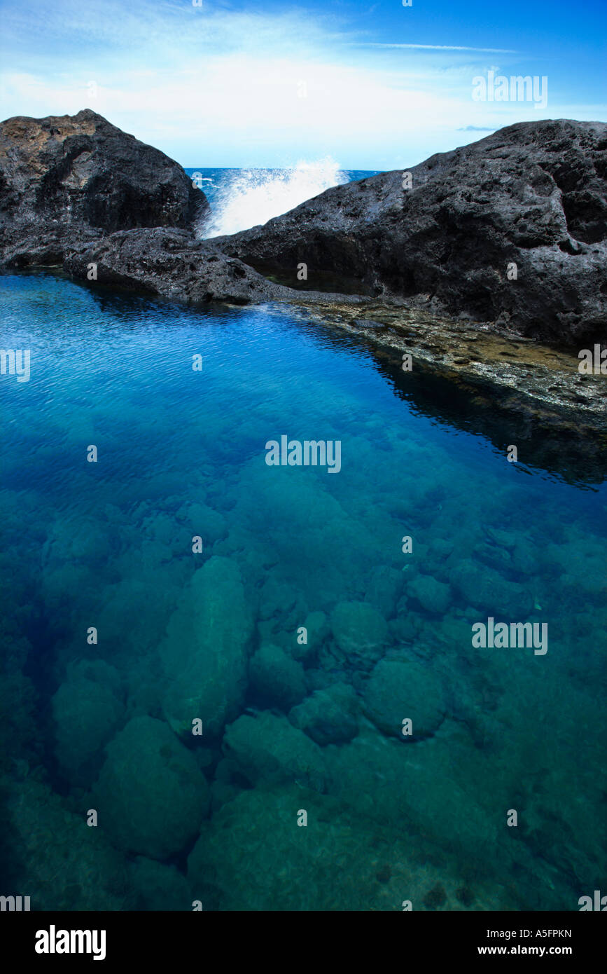 Tidal pool with wave crashing on rocks in background with blue sky in ...