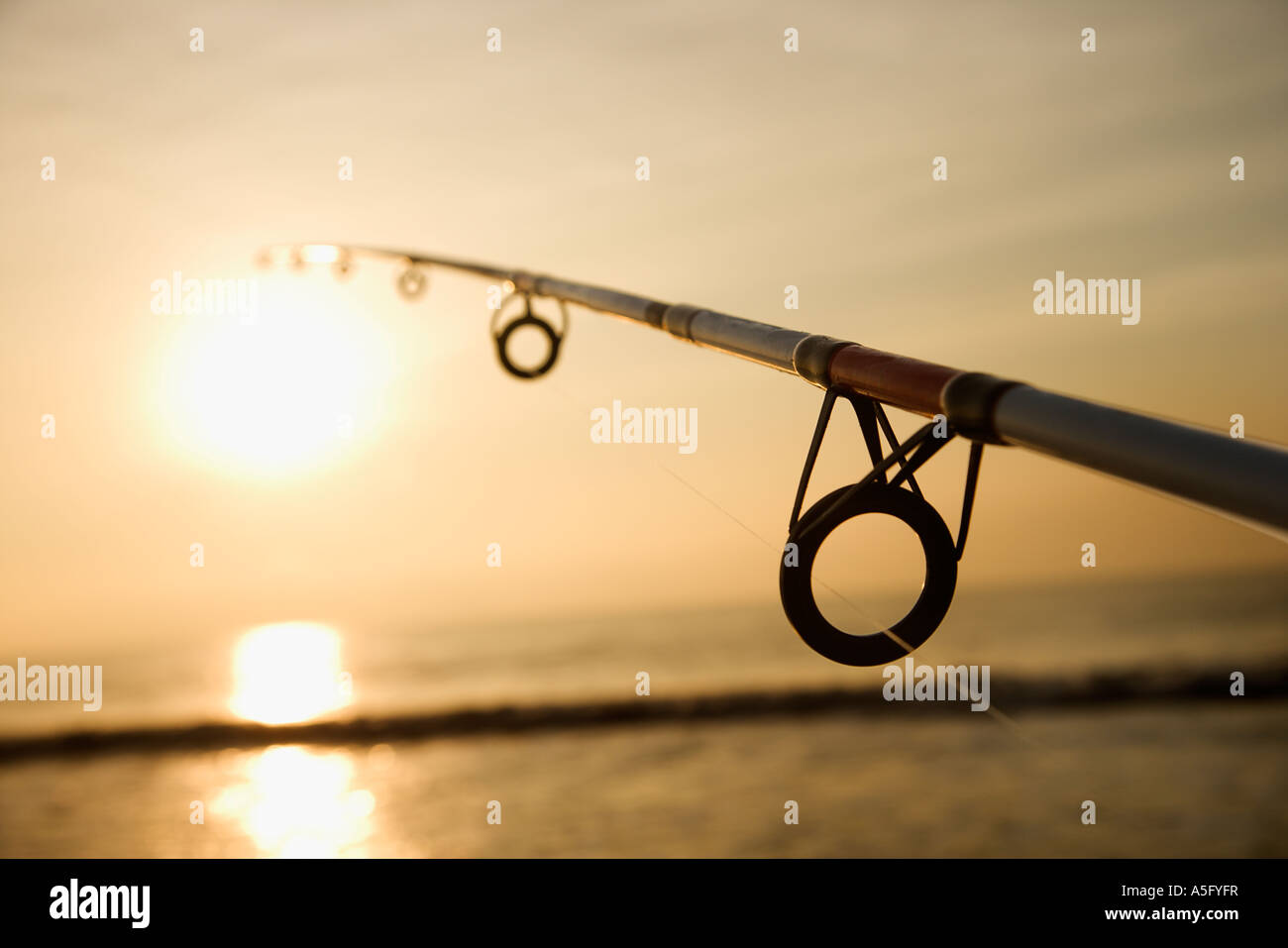 Fishing pole against ocean at sunset Stock Photo - Alamy