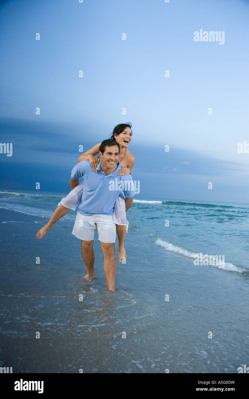 Caucasian mid adult male carrying female piggyback style on beach Stock ...