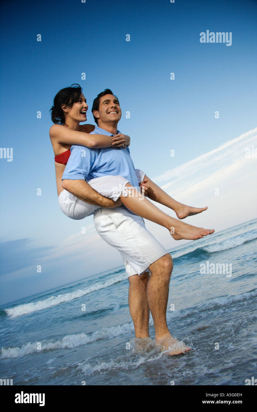 Caucasian mid adult male carrying female piggyback style on beach Stock ...